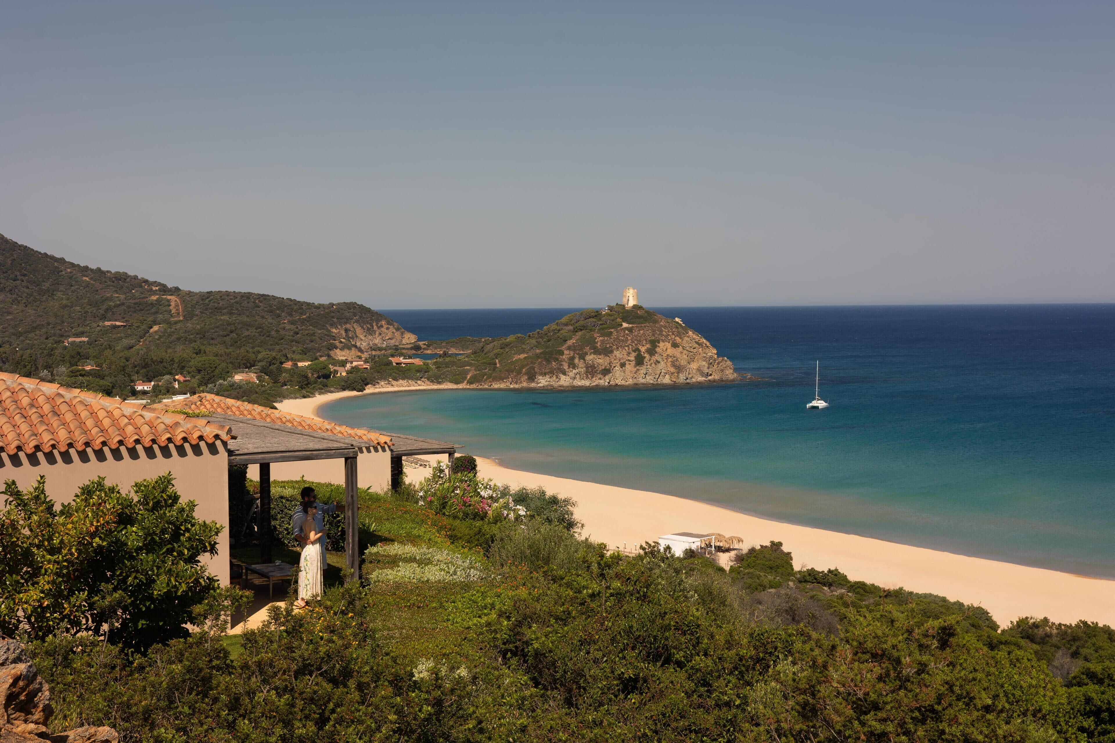 Paisagem costeira com uma praia, um farol e um edifício com telhado em azulejos.