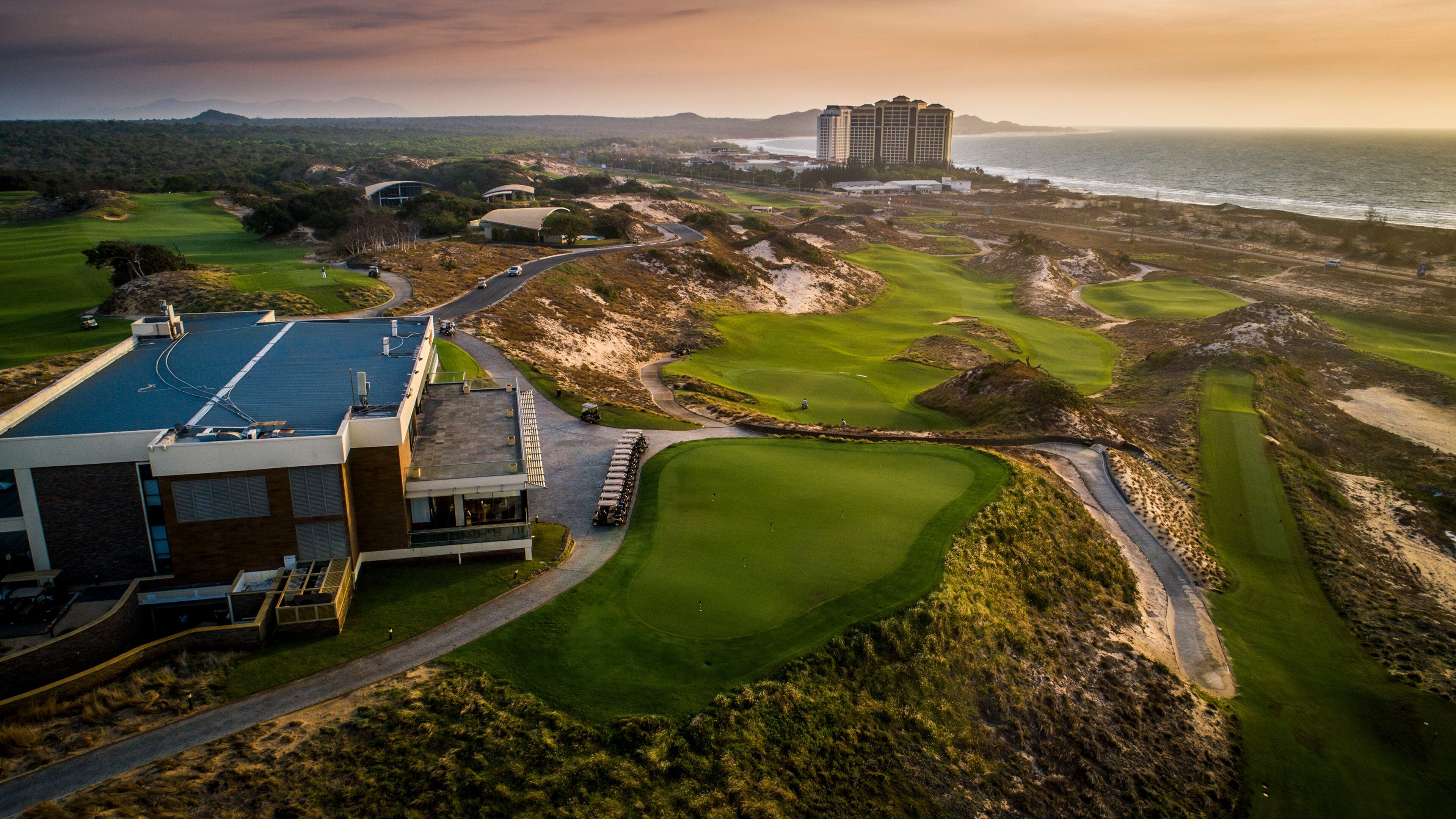 Um campo de golfe com um clube, uma área de estacionamento e vista para o oceano.