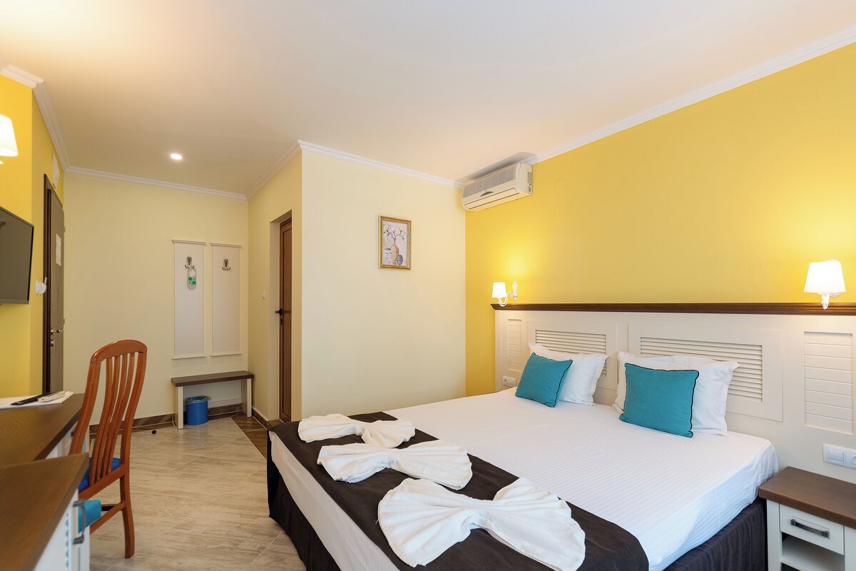 Quarto de hotel com cama, escrivaninha, cadeira, banco e ar condicionado.