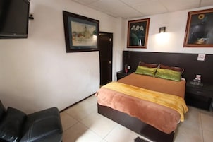 Quarto com cama, mesa de cabeceira, cadeira e porta.