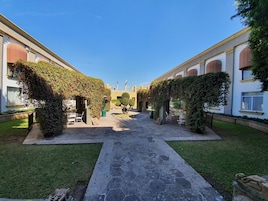 Um pátio central com um caminho de pedra, rodeado por edifícios com janelas em arco cobertas de hera.