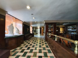 Um hall de hotel com piso xadrez, uma estátua e um balcão de recepção.