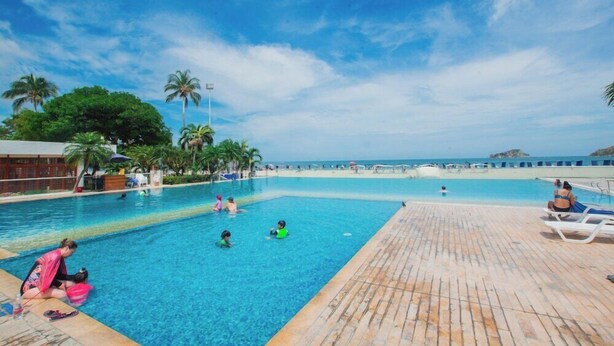 Piscina com água azul cristalina, rodeada por palmeiras e um deck de madeira.
