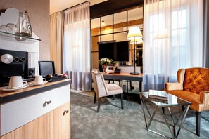Quarto de hotel com cozinha compacta, área de jantar e sala de estar com sofá e poltrona.