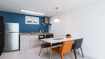 Cozinha compacta com geladeira, pia e fogão, mesa de jantar com cadeiras e uma luminária pendente.
