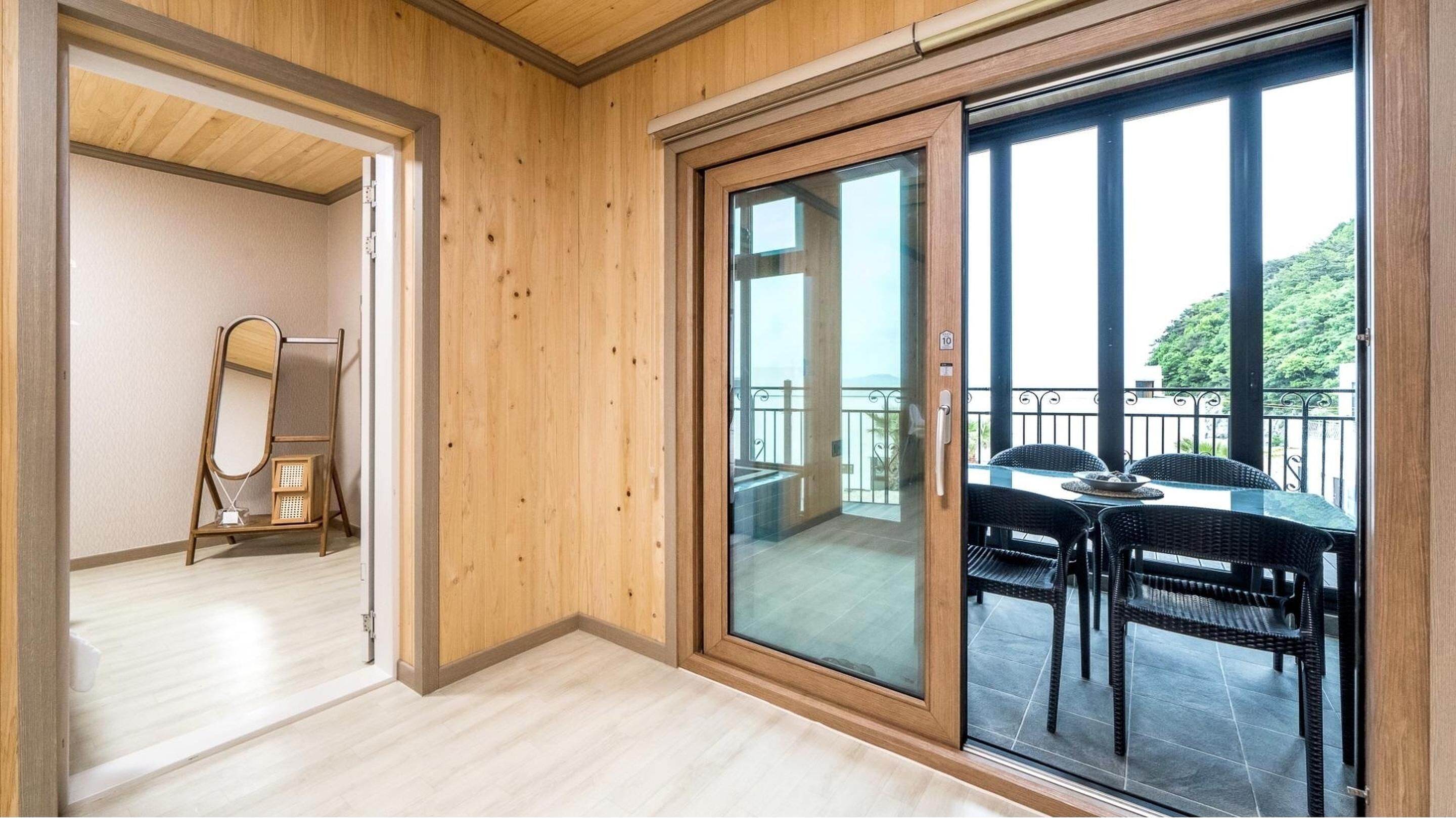 Quarto com decoração em madeira, porta de vidro deslizante para uma varanda externa com mobiliário de vime.
