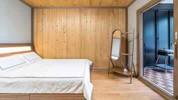 Quarto com parede de ripas de madeira, cama com roupa de cama branca, espelho de corpo inteiro e uma pequena mesa com bandeja.