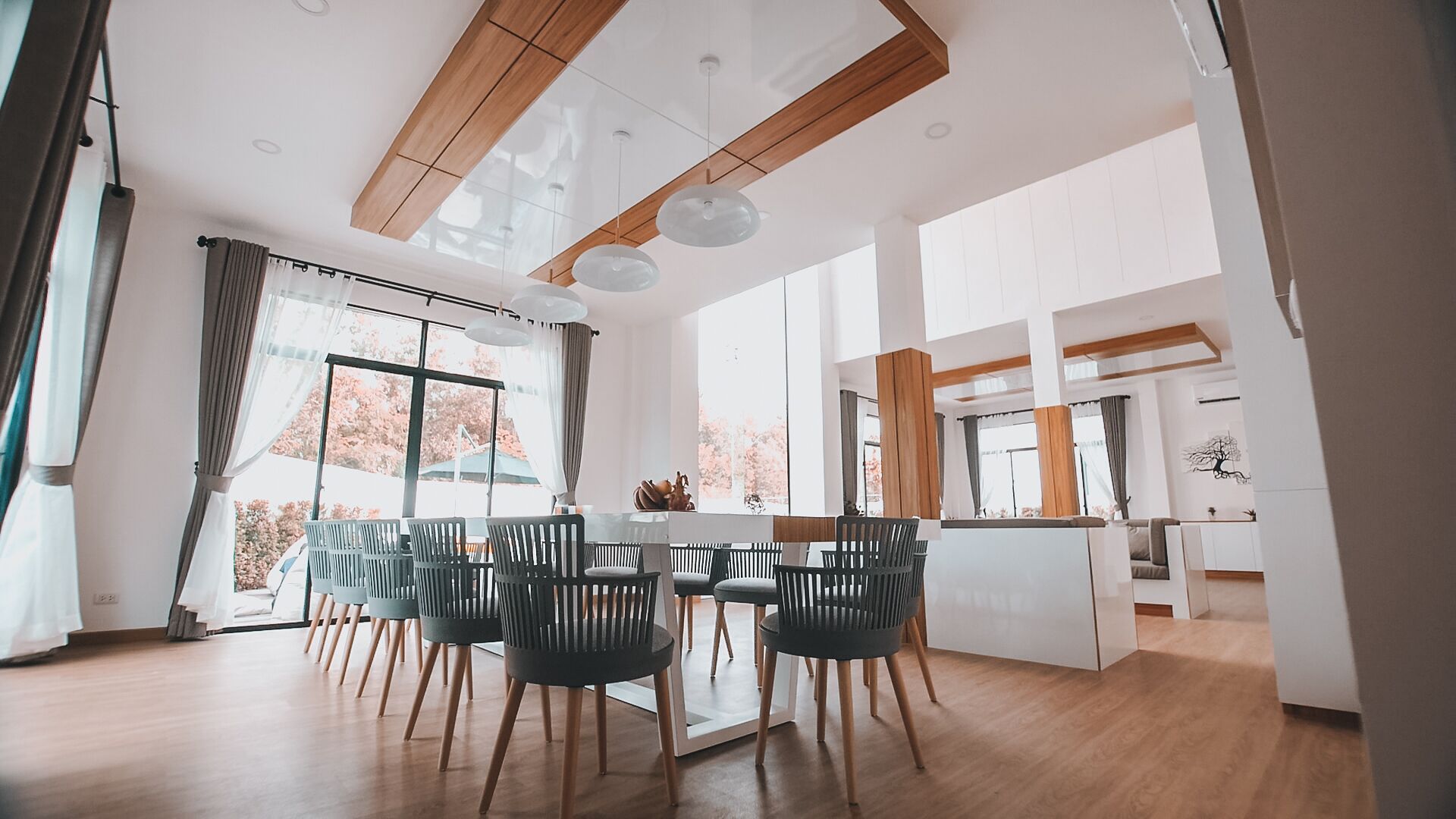 Uma sala de jantar moderna com teto de madeira, janelas amplas e vista para árvores.