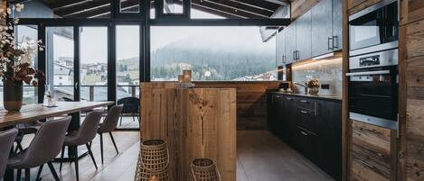 Uma cozinha moderna com detalhes em madeira, grandes janelas e vista para as montanhas.