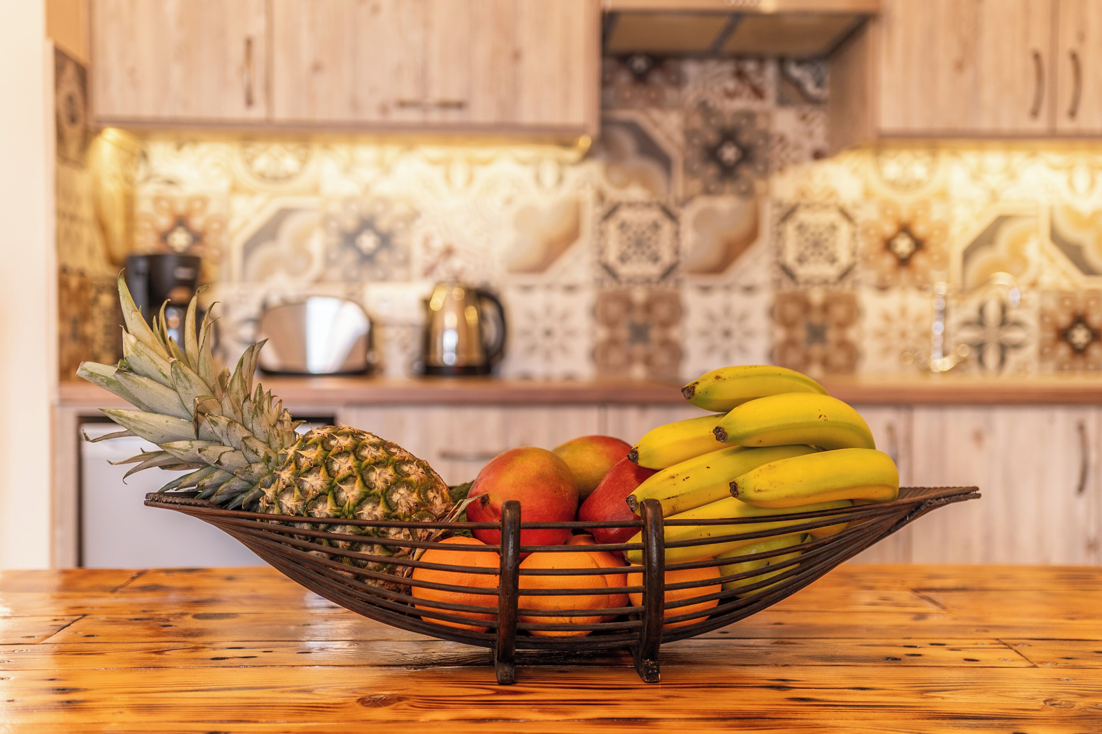 Uma mesa de madeira com uma fruteira contendo abacaxi, manga e bananas.