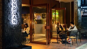 Restaurante com entrada por porta de vidro, mesas ao ar livre e letreiro luminoso.