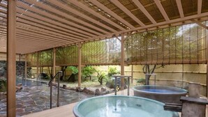 Uma onsen japonesa tradicional com piso de madeira, caminhos de pedra e paredes de bambu.
