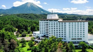 Um hotel moderno com telhado plano, rodeado por vegetação exuberante e uma montanha ao fundo.