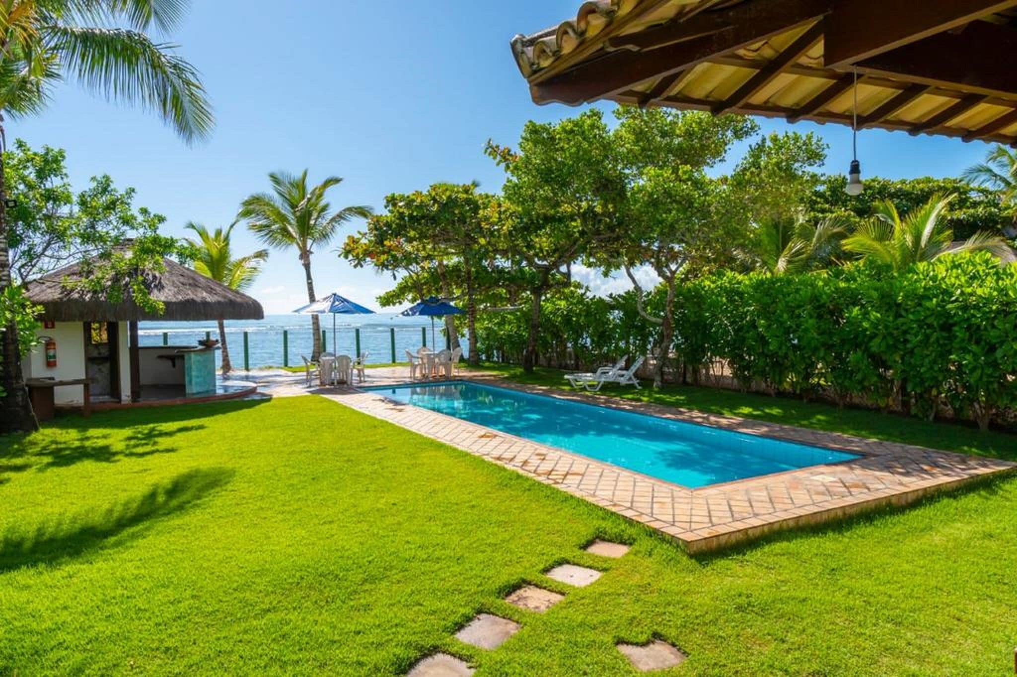 Uma piscina com um deck ao redor, um pequeno edifício e vegetação exuberante.