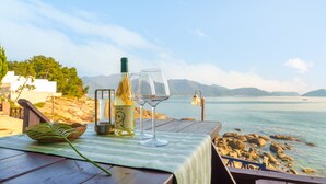 Uma mesa com uma garrafa de vinho, duas taças de vinho e uma vela sobre uma mesa de madeira, em frente a uma paisagem costeira deslumbrante.