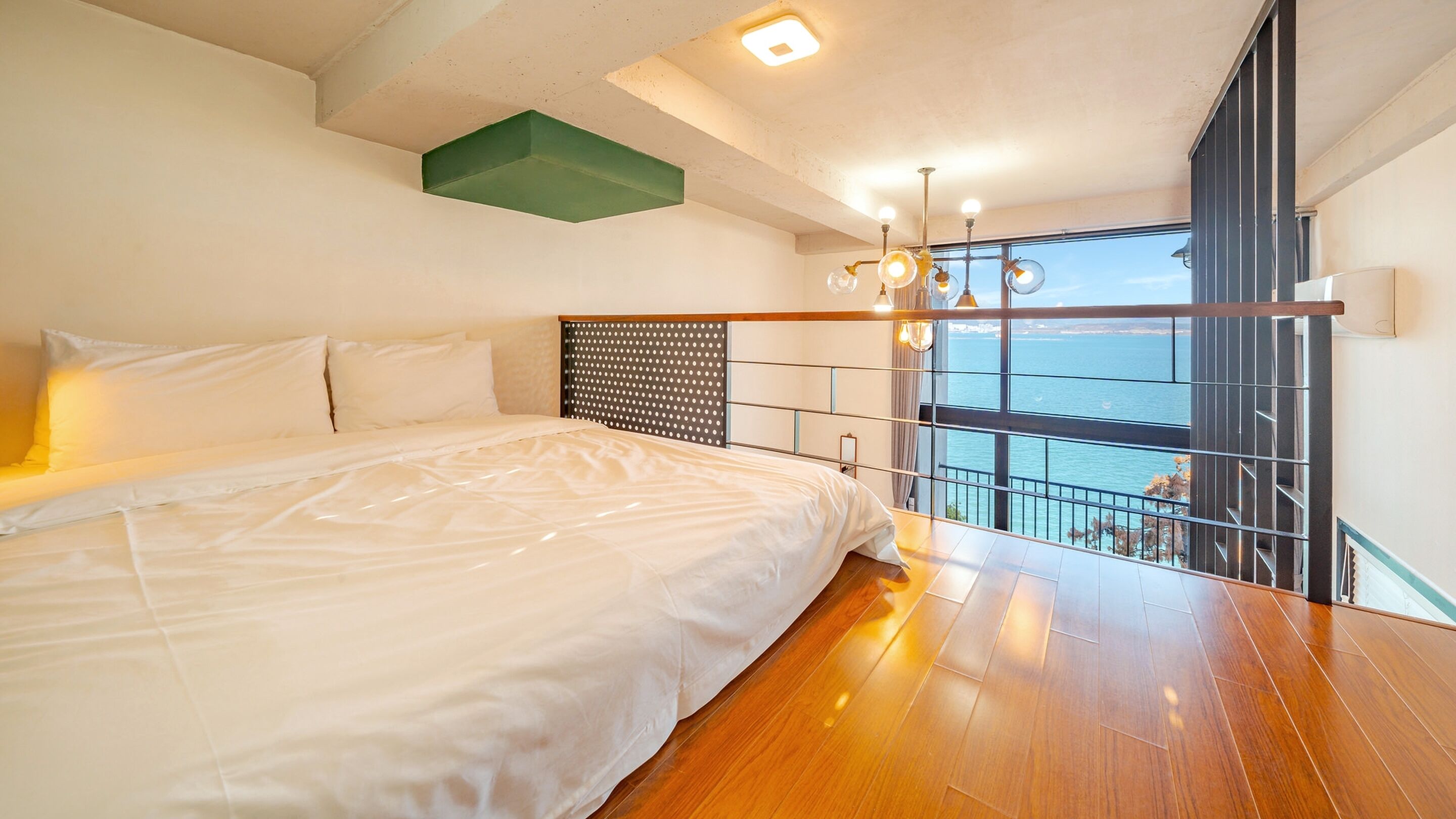 Quarto com cama grande, vista para o mar e varanda com guarda-corpo.