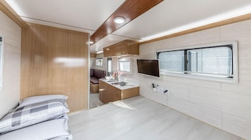 Interior compacto de RV com cozinha compacta, cama e janela com vista para uma parede de tijolos.