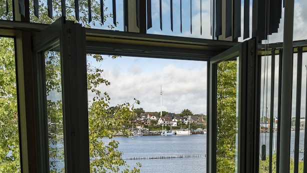 Quarto com uma grande janela com vista para um lago, varanda com corrimão e vista para casas do outro lado da água.