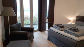 Quarto com cama, cadeira, abajur e vista para o exterior através de uma janela grande.