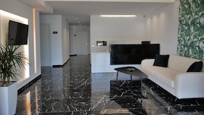 Um lobby de hotel moderno com piso de mármore, um sofá branco, uma TV de tela plana e um balcão de recepção.
