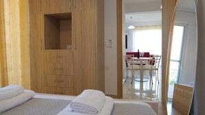 Quarto de hotel com cama, guarda-roupa de madeira, zona de refeições visível por uma porta aberta e um espelho grande.