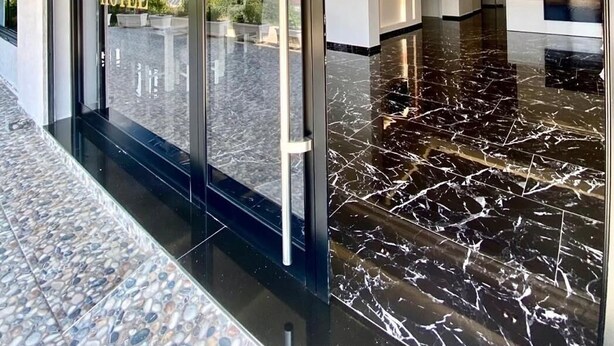 Entrada de hotel moderna com fachada de vidro, piso de mármore e vista para a paisagem urbana.