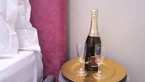 Uma garrafa de champanhe sobre uma mesa redonda com dois copos, toalha de mesa branca e cortina rosa.
