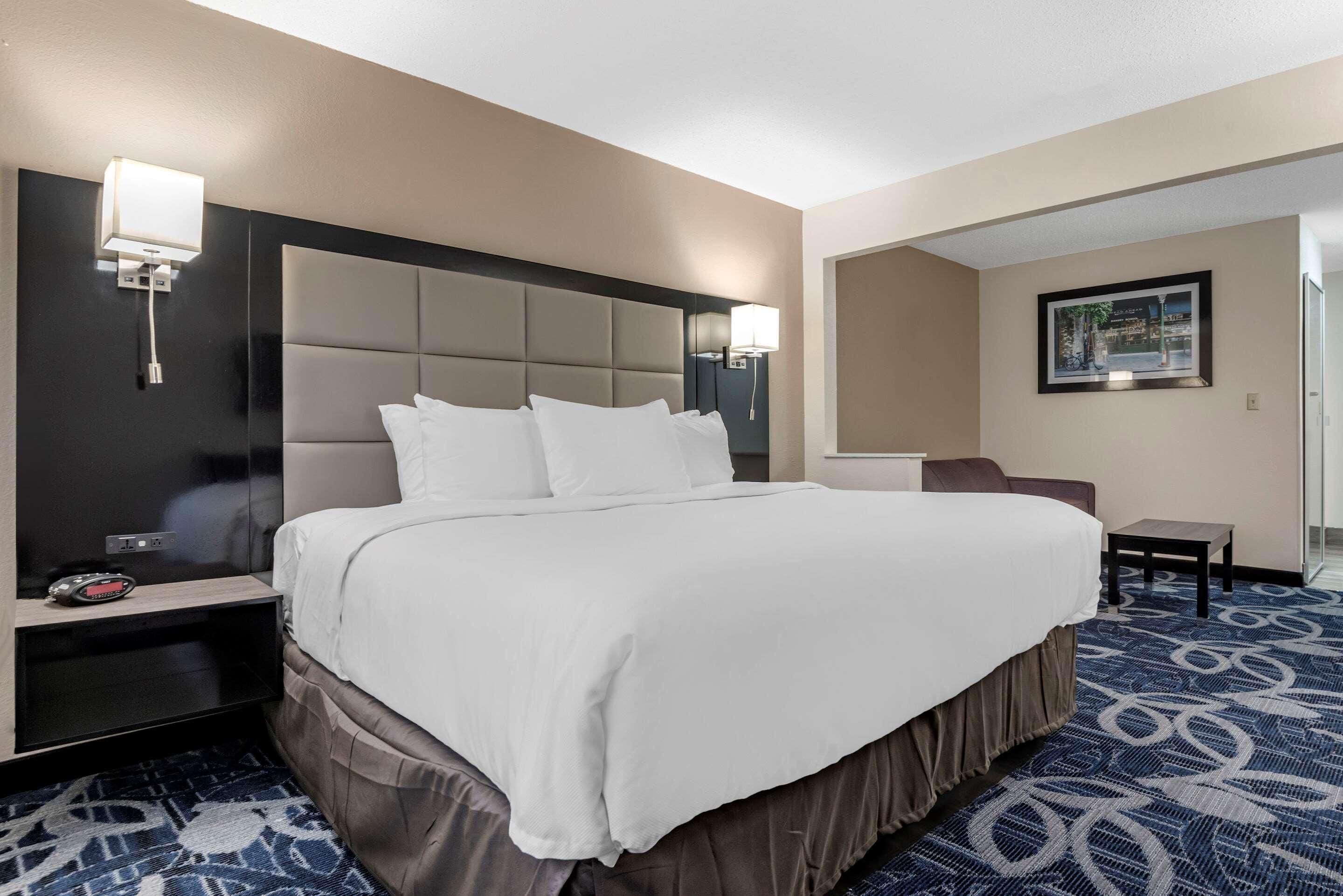 Quarto de hotel com uma cama grande, mesas de cabeceira, escrivaninha e uma cadeira.