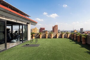 Terraço com grama sintética, equipamentos de ginástica e plantas em vasos.