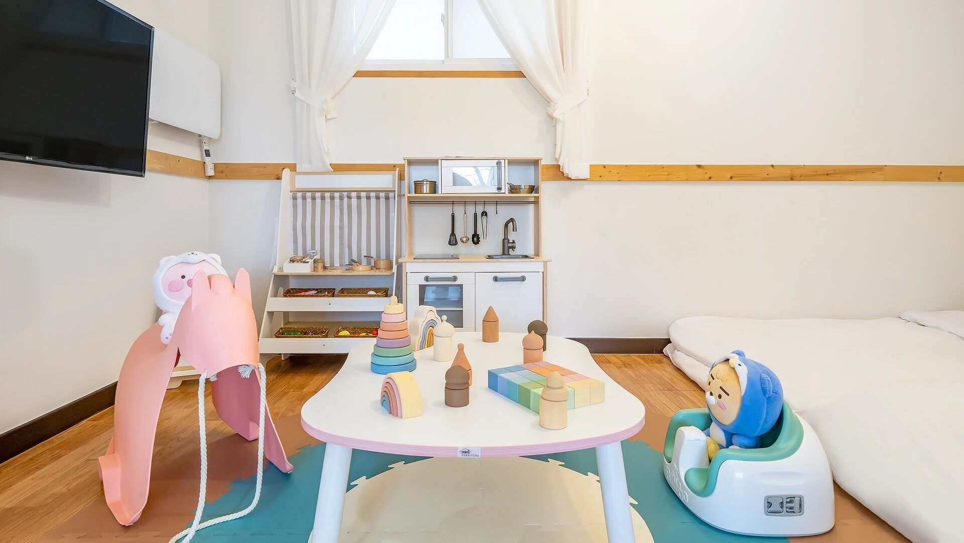 Espaço infantil com mesa, brinquedos, berço e televisão.
