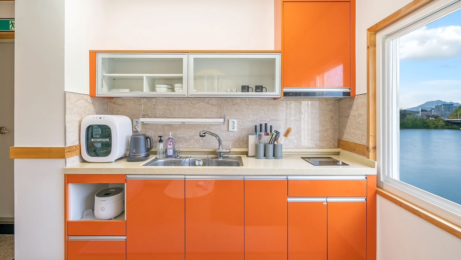Cozinha compacta com armários laranja, micro-ondas, chaleira e pia.