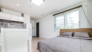 Quarto com cama, janela com vista, cozinha compacta e porta para outro espaço.