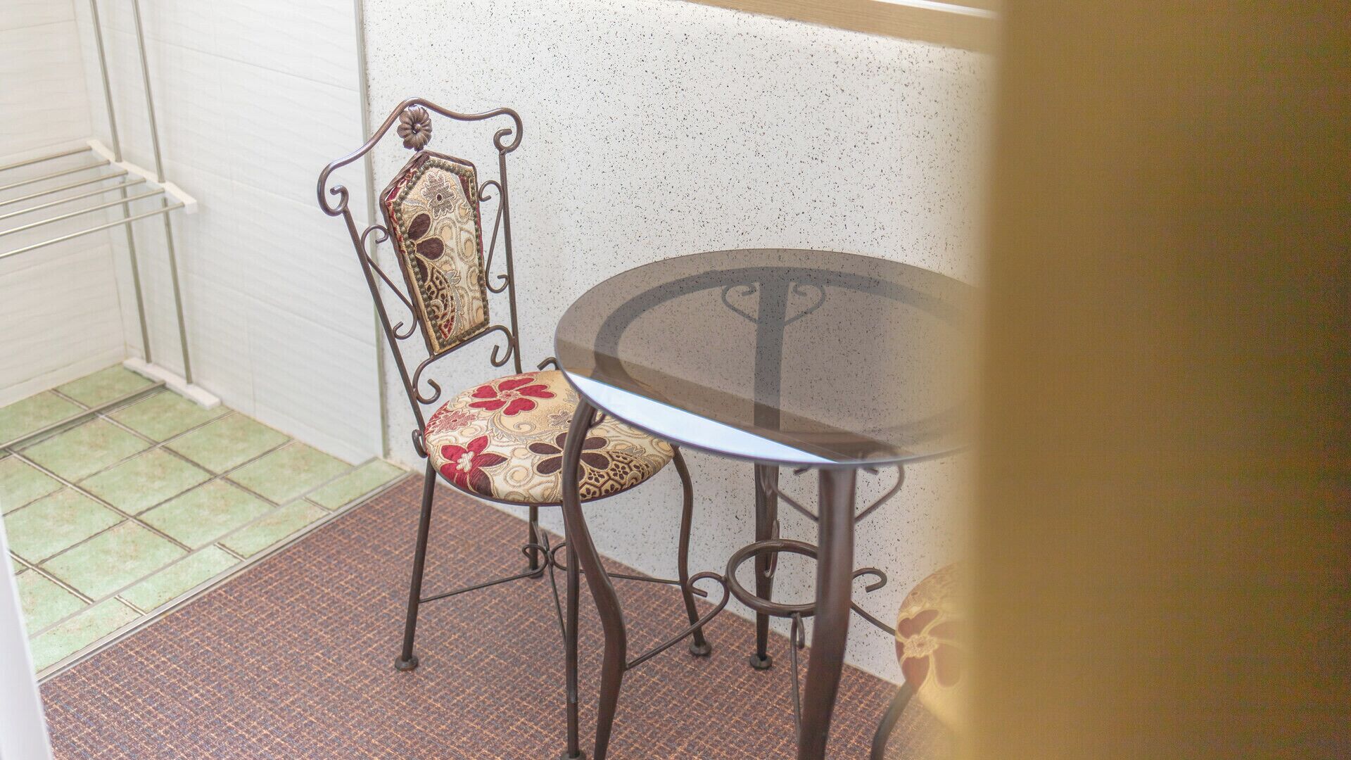 Um canto com uma cadeira e mesa de metal, chão de azulejos e parede branca.