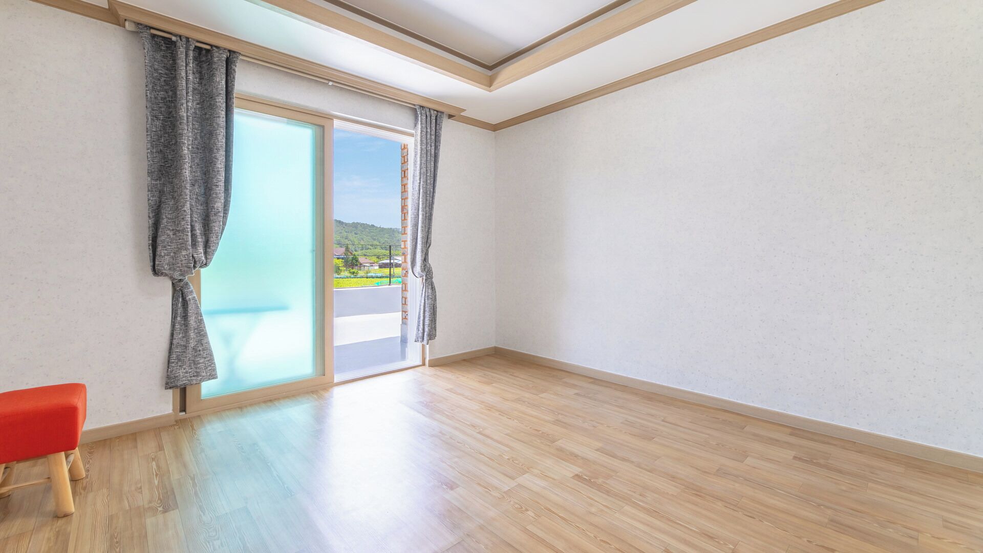 Um quarto com piso de madeira, uma cadeira vermelha e vista por uma porta de vidro.