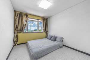 Quarto com cama, cortinas, janela e vista para o verde lá fora.