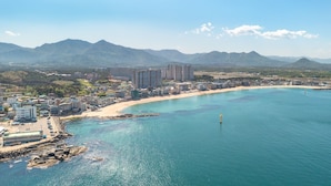 Paisagem costeira com praia, edifícios e montanhas ao fundo.
