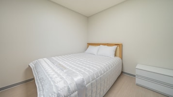 Quarto com cama, cabeceira de madeira, mesa de cabeceira branca e aparador.
