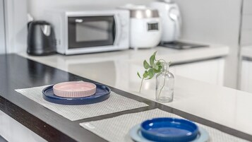 Uma bancada de cozinha com micro-ondas, chaleira e uma pequena planta em vaso.