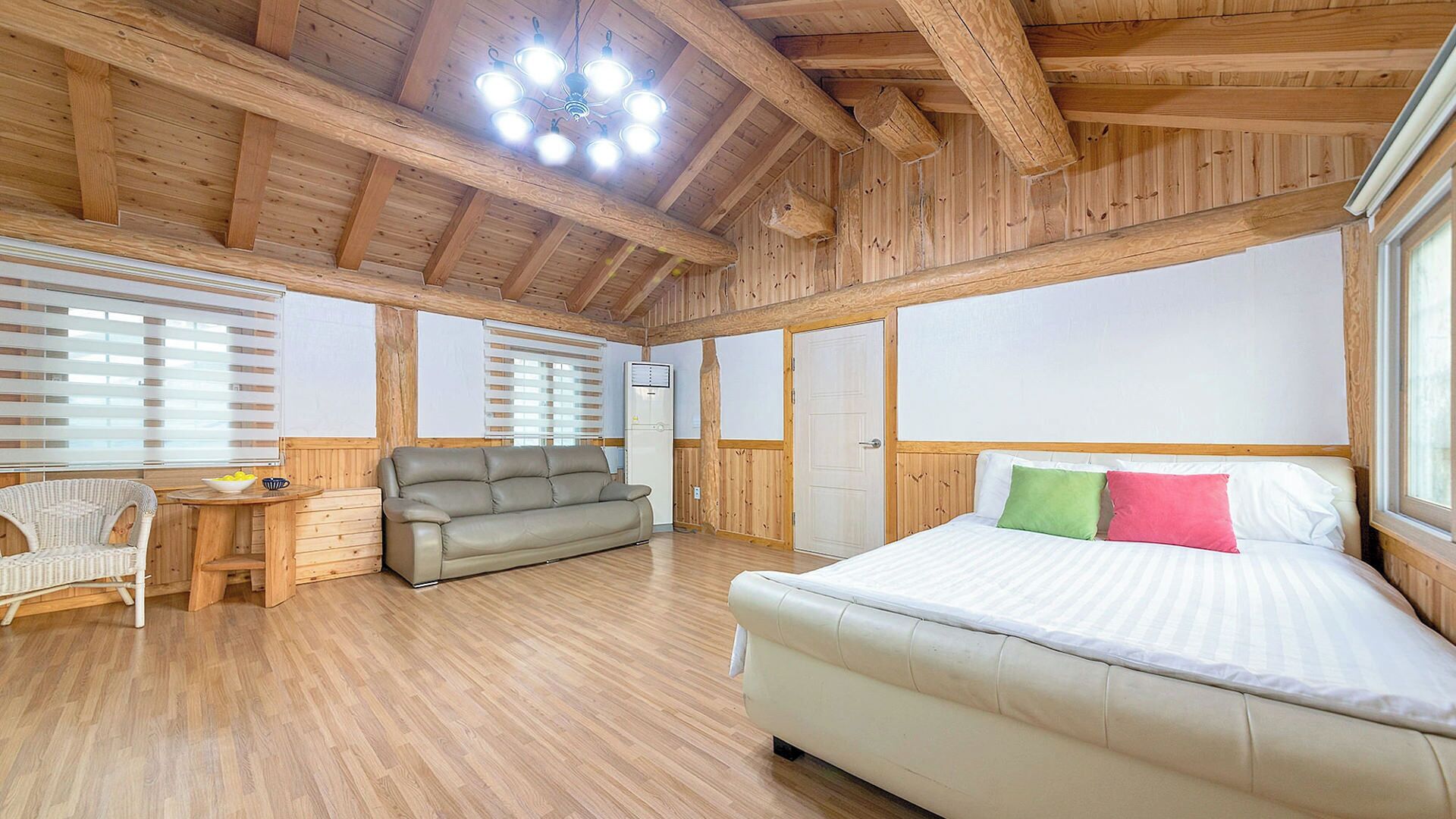 Quarto com cama, sofá, poltrona, mesa pequena e janela com persianas.