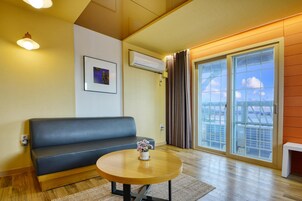 Uma sala de estar moderna com um sofá, uma mesa redonda de madeira com um vaso, um ar condicionado e amplas portas de vidro deslizantes com vista.
