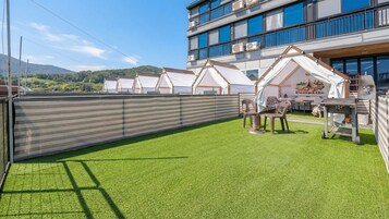 Terraço com grama sintética, churrasqueira e estrutura tipo tenda.