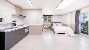 Quarto de hotel moderno com cozinha compacta, cama com estrutura tipo tenda e grande janela com vista.