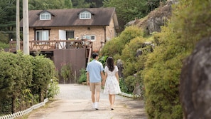 Um casal caminhando por um caminho de cascalho em direção a uma casa de tijolos com varanda de madeira.