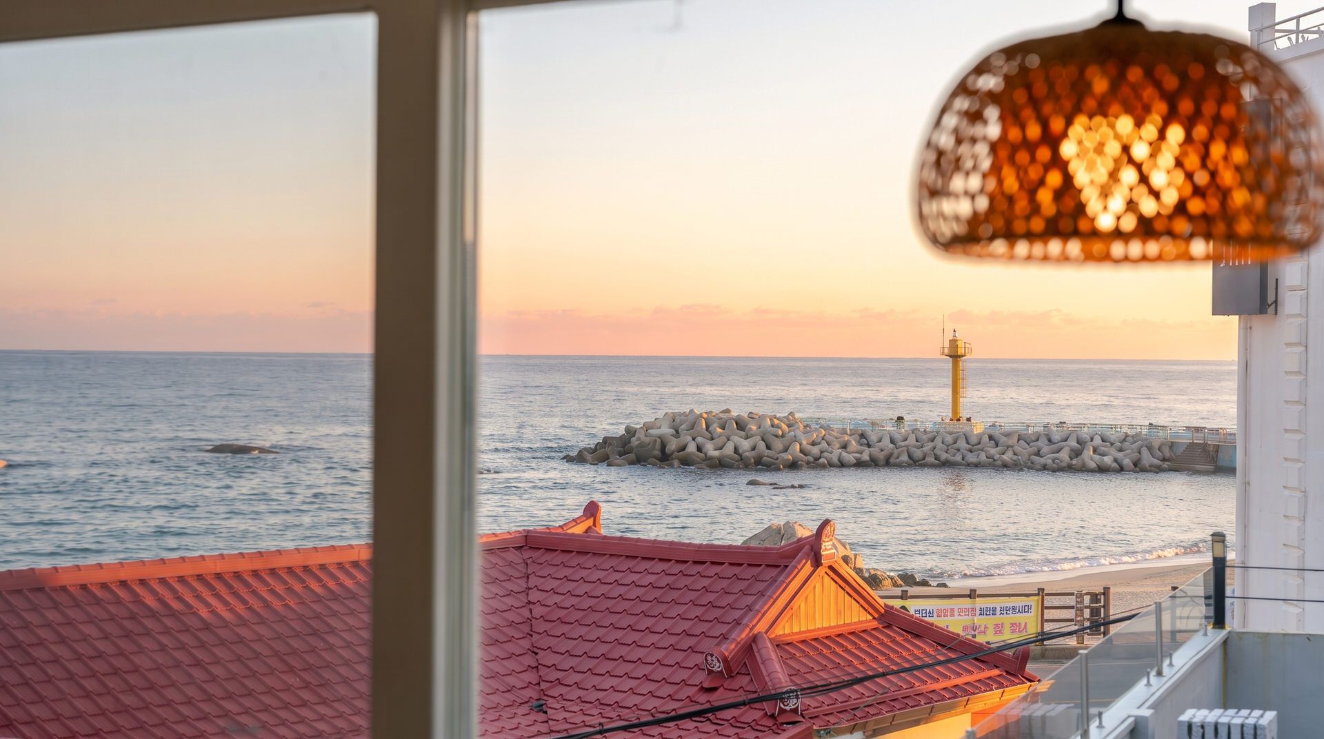 Vista costeira com farol, um edifício de telhado vermelho e um candeeiro suspenso.