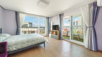 Quarto de hotel moderno com uma cama grande, TV e varanda com vista para a praia.