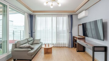 Uma sala de estar moderna com um sofá, uma mesa de centro, uma TV de tela plana e uma janela grande com cortinas.