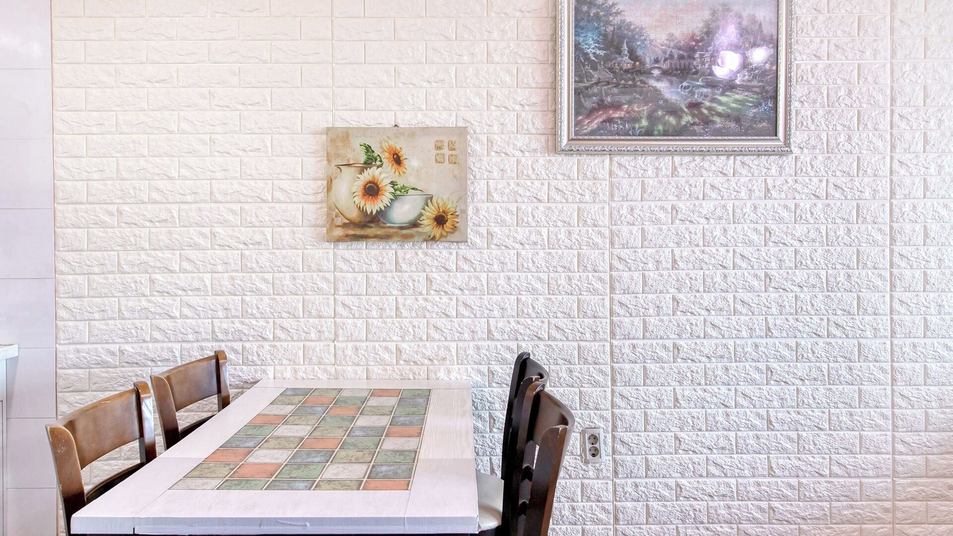 Uma área de refeições com parede de tijolos brancos, uma mesa com toalha de mesa colorida e duas cadeiras.