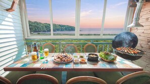 Uma mesa posta para refeição com vista para o mar, um churrasco e uma garrafa de cerveja.