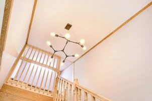 Uma escadaria com guarda-corpos de madeira e um lustre moderno com várias lâmpadas.