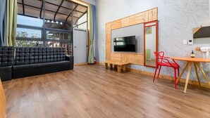 Quarto moderno com sofá de couro preto, um banco de madeira, uma cadeira vermelha, televisão e mesa de madeira.